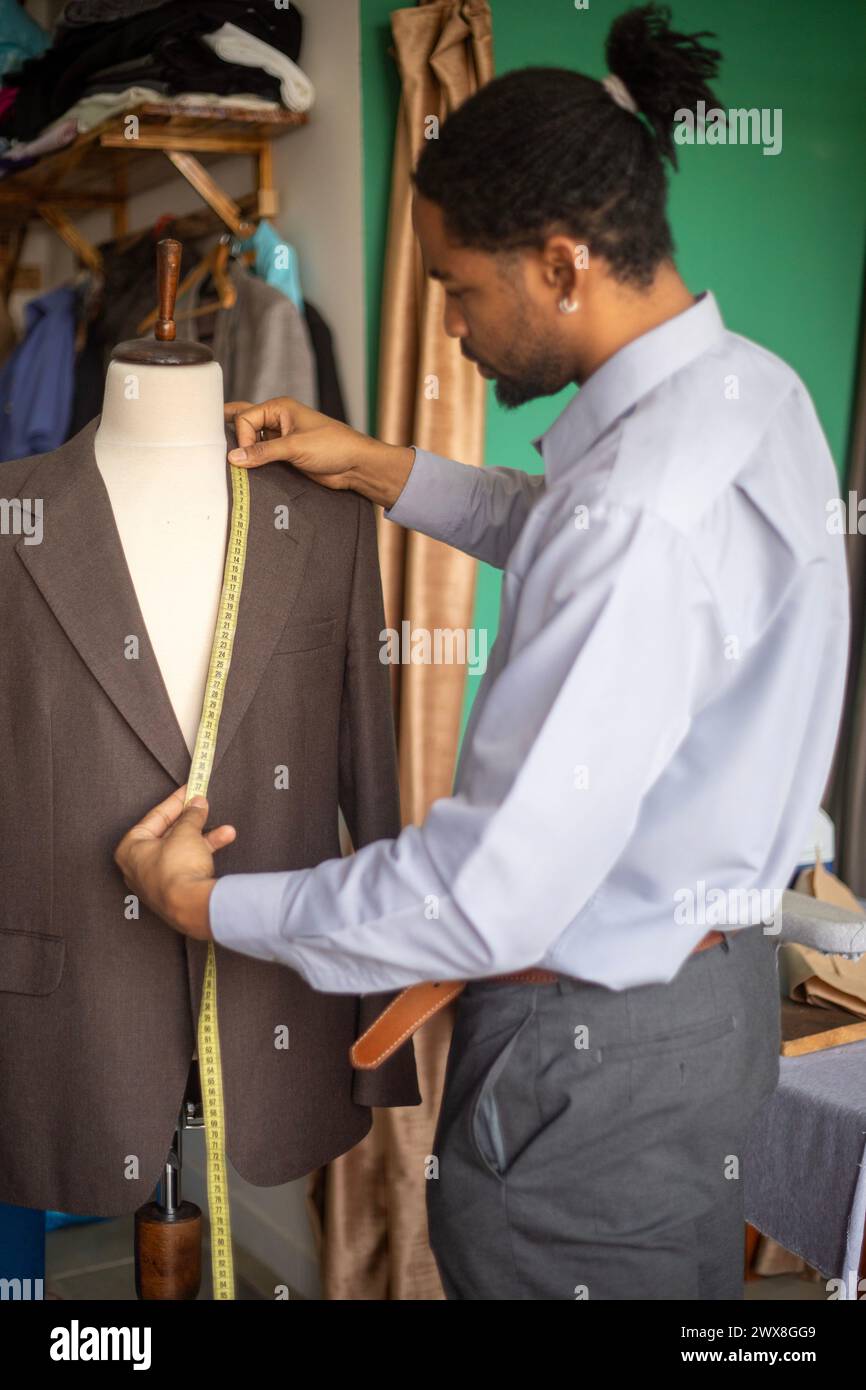 Young African American tailor at work measuring and marking jacket collar, Bespoke tailor at ...