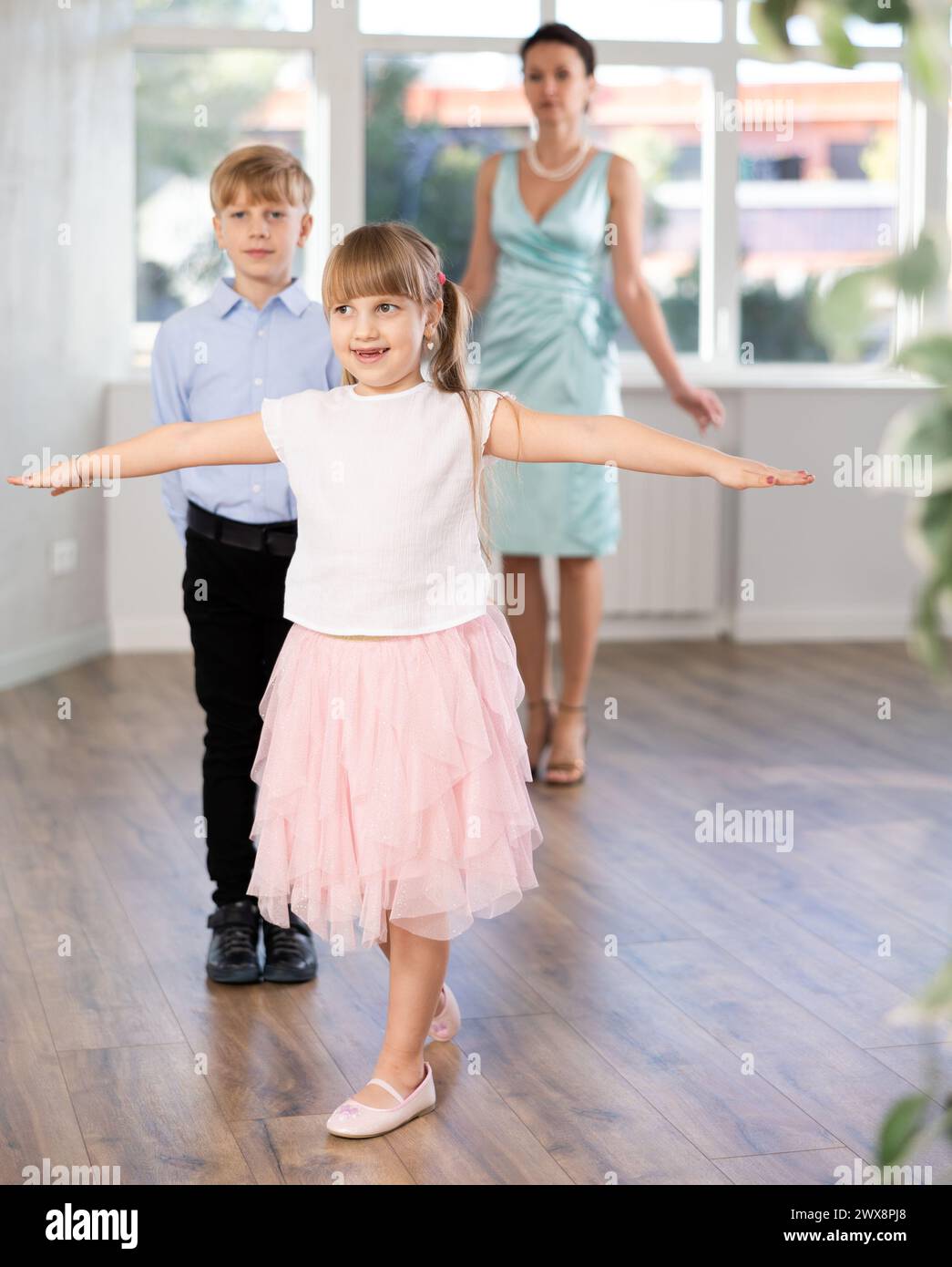 Girl rehearsing curtsey in dance hall with boy partner and female ...
