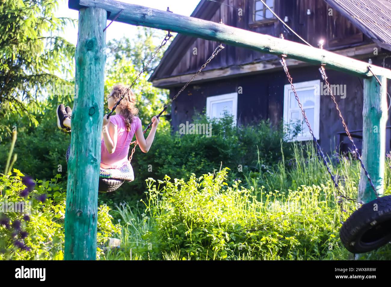 Happy childhood. A little girl swings on homemade swing in village ...