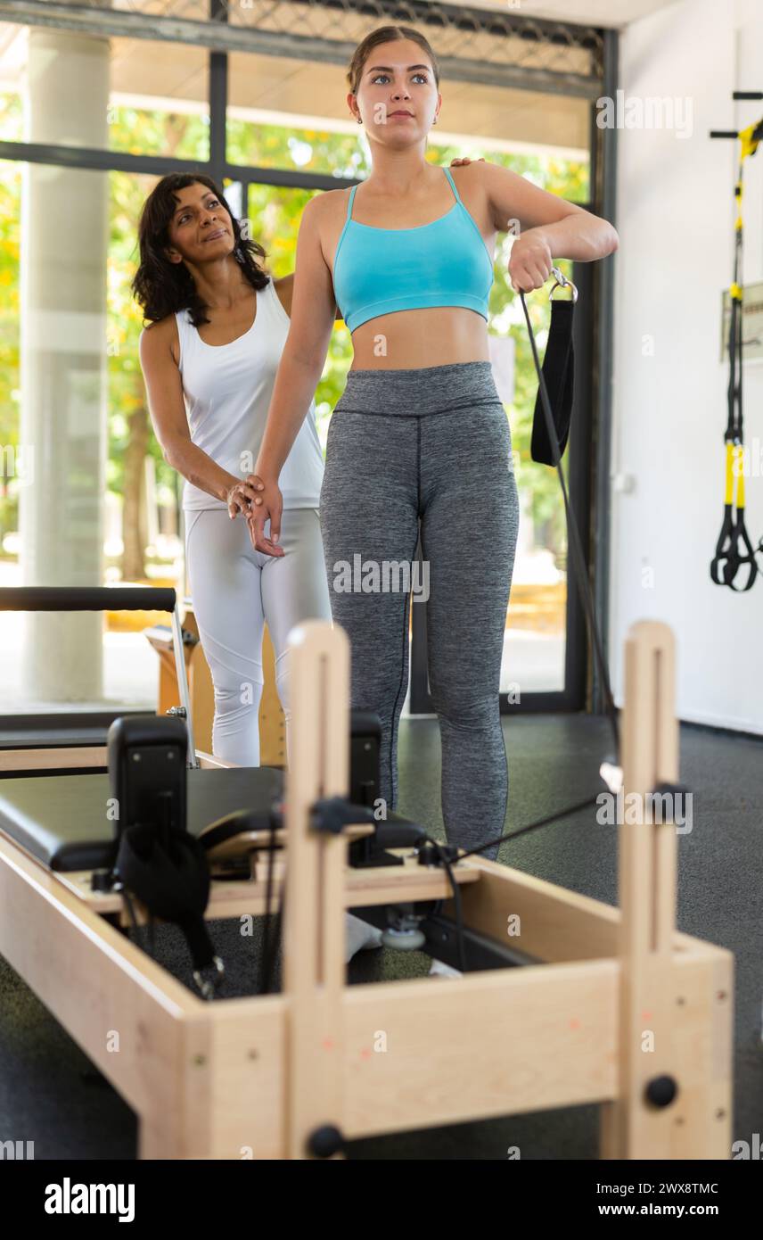 Focused Latin female instructor helping girl practicing pilates ...