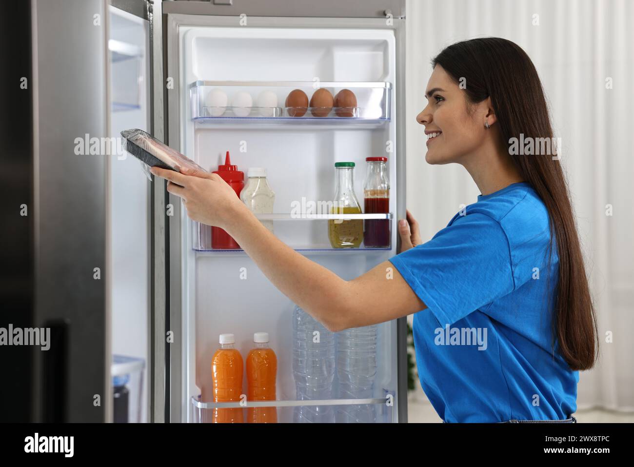 Young woman taking pack of meat out of refrigerator indoors Stock Photo ...