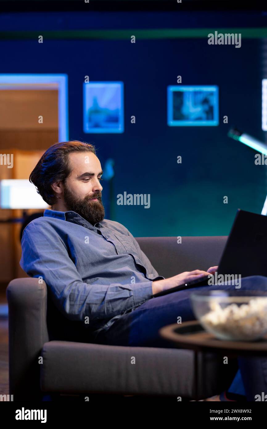 Smiling man enjoying bowl of popcorn while watching TV and solving ...