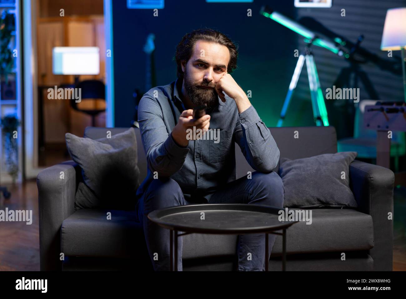 Tired man zapping through channels, watching news broadcast while ...