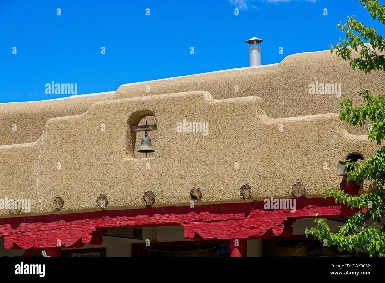 Cast bell on adobe walled roof pediment under bright blue sky in Taos ...