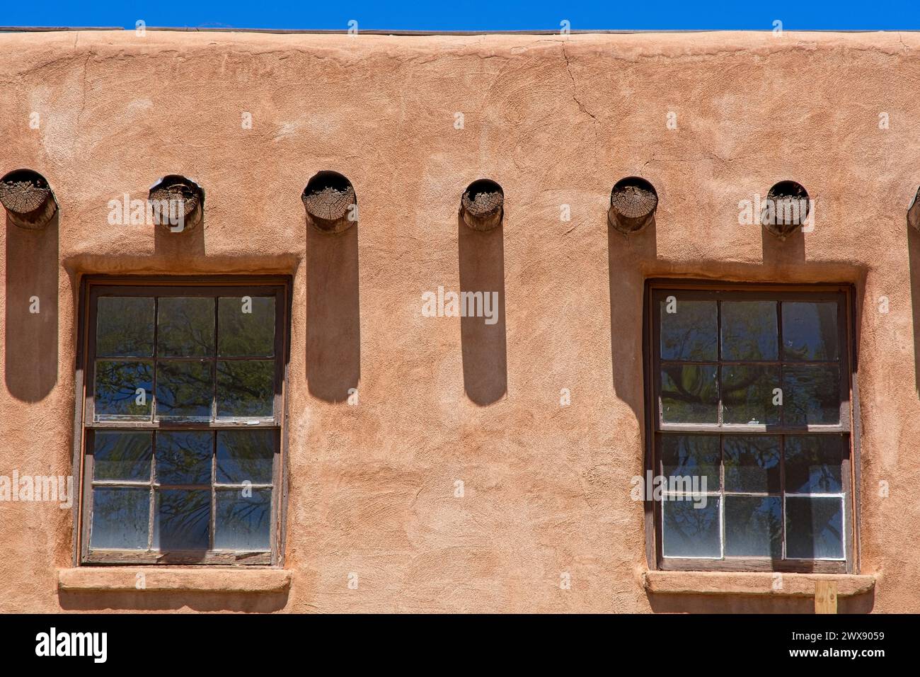 Close up rustic windows under row of exposed viga roof beams in adobe ...
