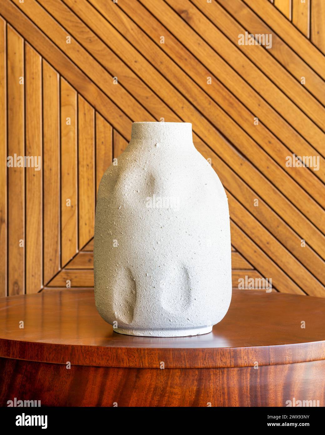 A textured white vase stands on a polished wood table, complemented by ...