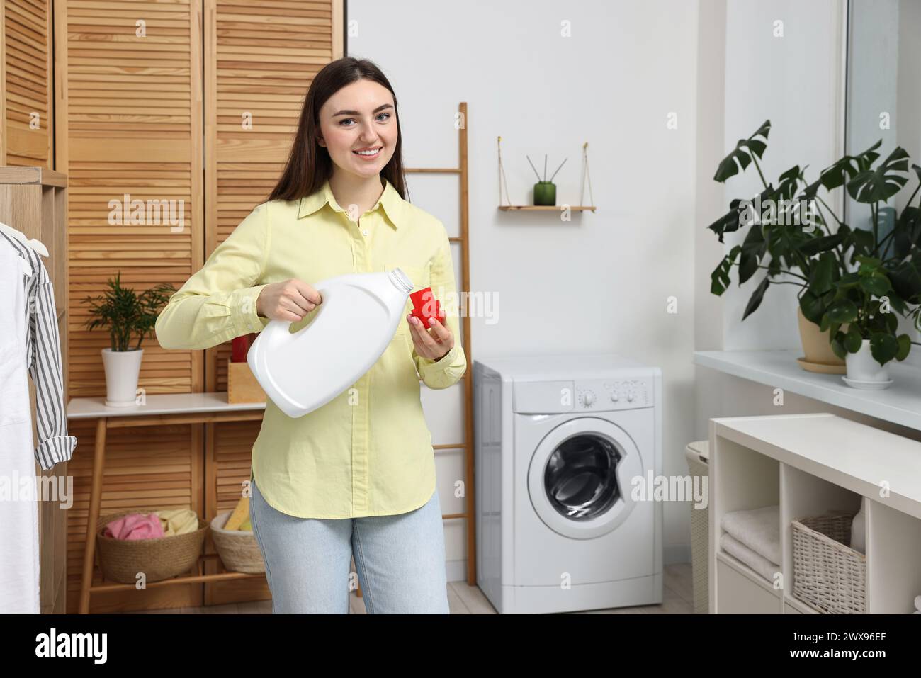 Beautiful young woman pouring detergent into cap in laundry room Stock ...
