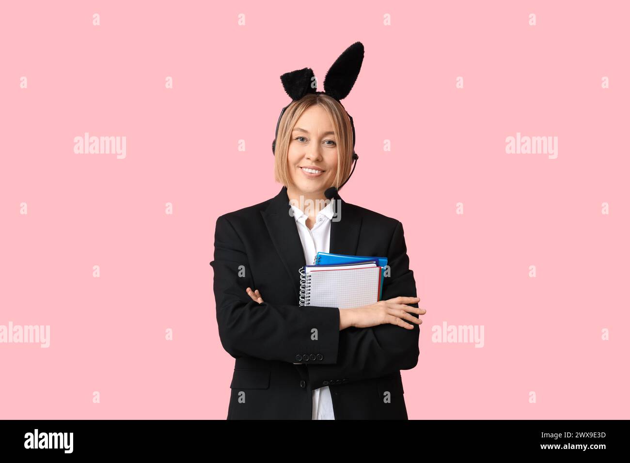 Happy adult female operator in bunny ears with headset and notebooks on ...