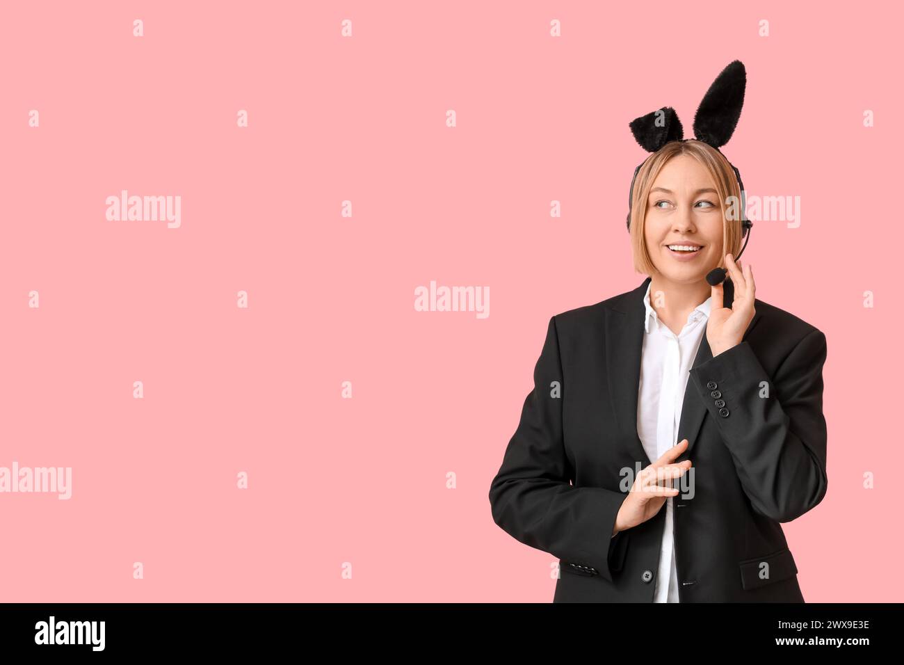 Happy adult female operator in bunny ears with headset on pink ...