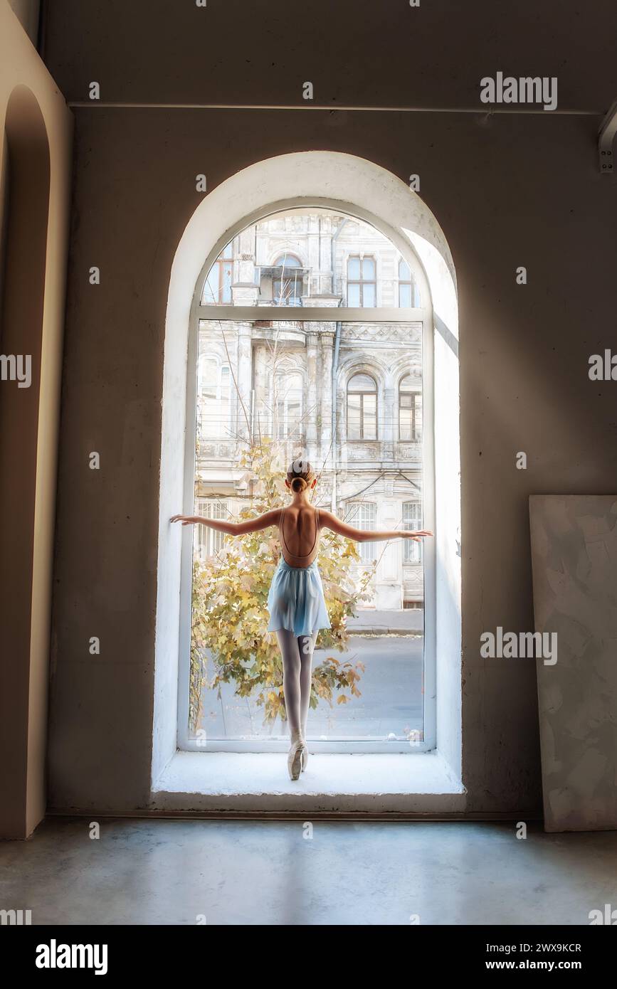 Young ballerina stands en pointe, back to the camera, framed by an ...