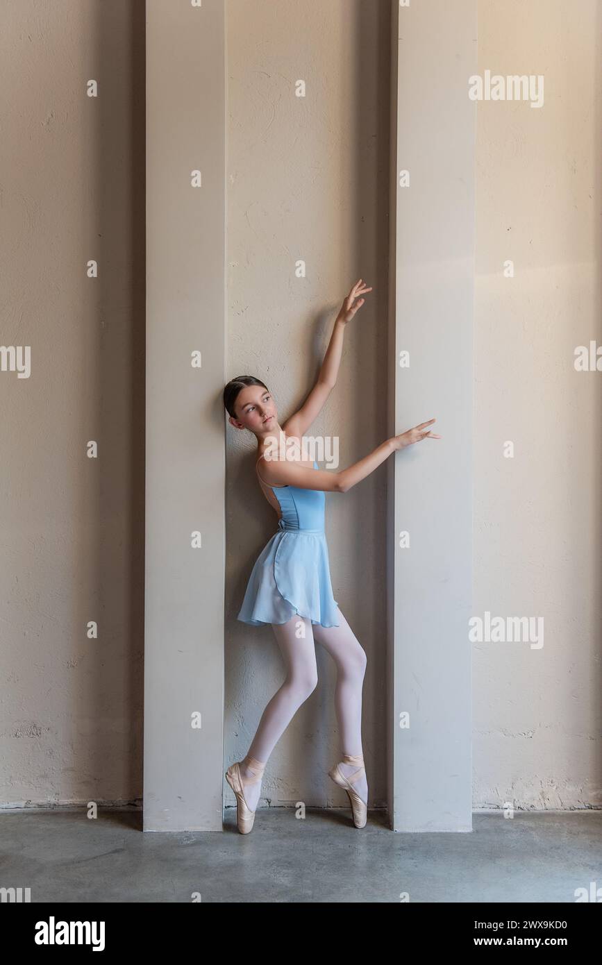 Elegant young ballerina in blue costume stands en pointe, arms raised ...