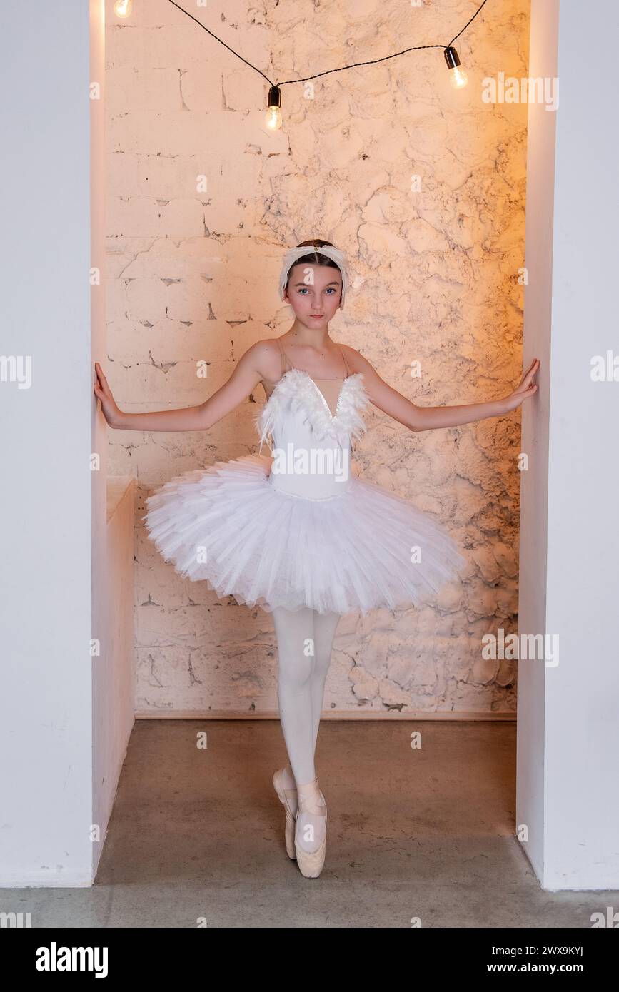 Poised young ballerina stands en pointe in hallway arch with warm ...