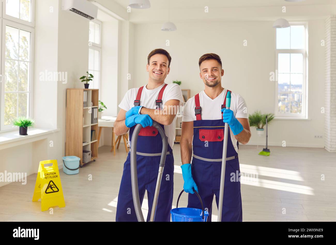 Happy janitors in uniform from professional cleaning service looking at ...