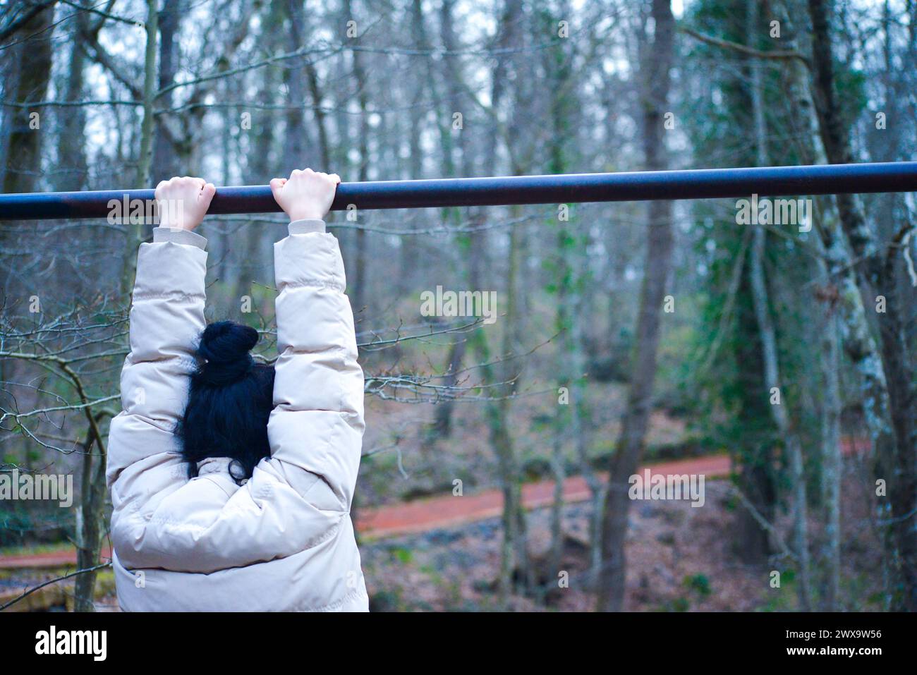 A woman engaging in outdoor fitness, hanging and stretching on a bar ...