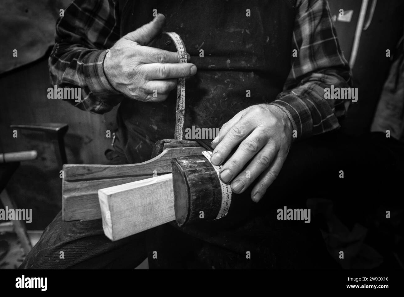 A grayscale of a shoemaker repairing shoes and measuring with meters ...