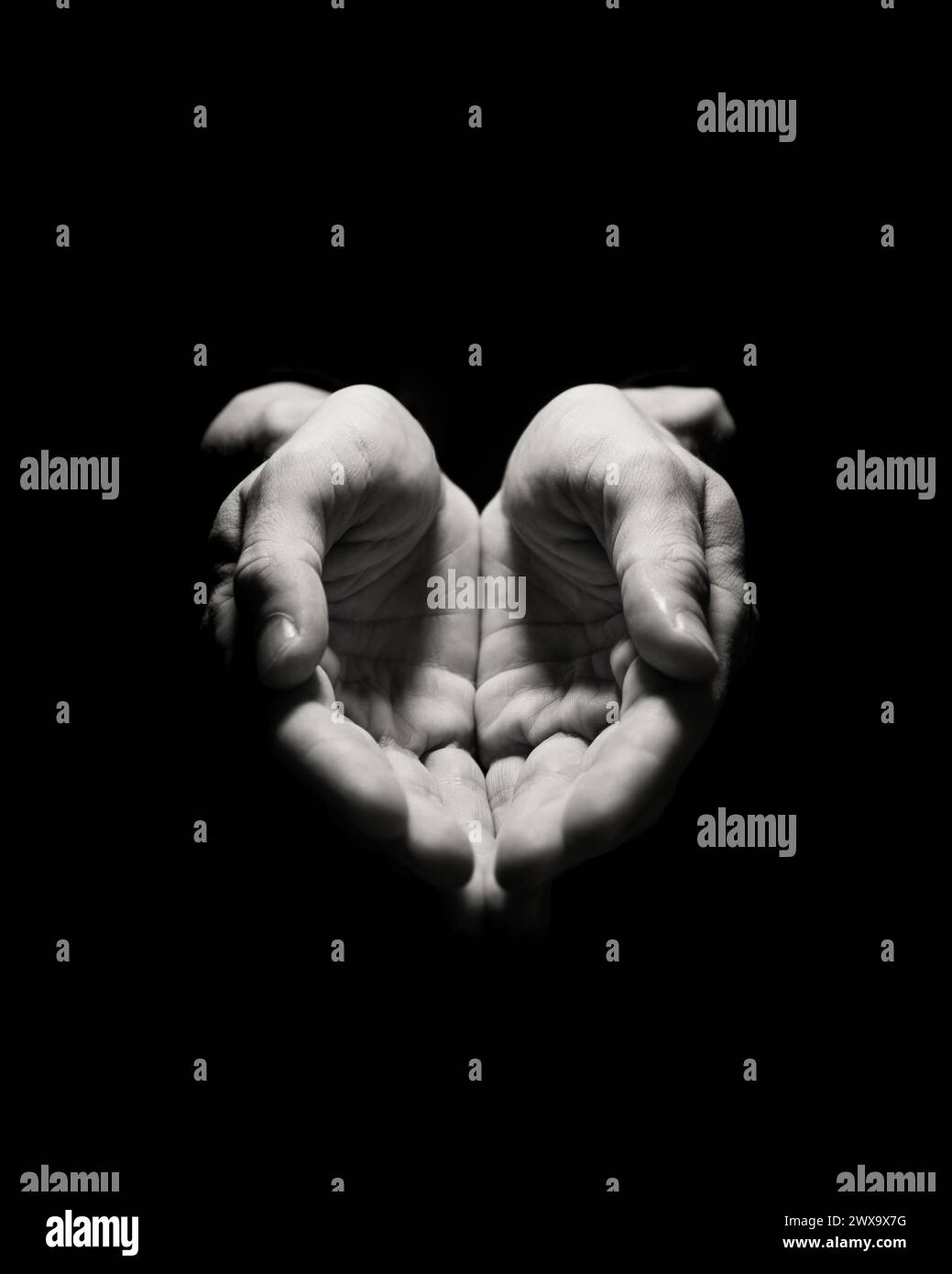 Human hands open in a gesture of giving, presented in stark black and ...