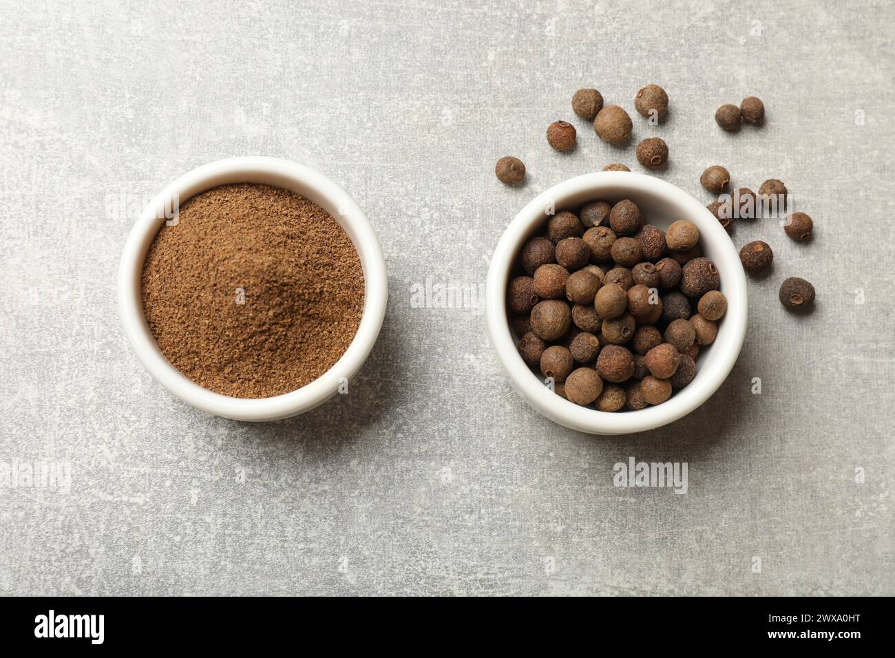 Ground allspice pepper and grains in bowls on grey table, top view ...