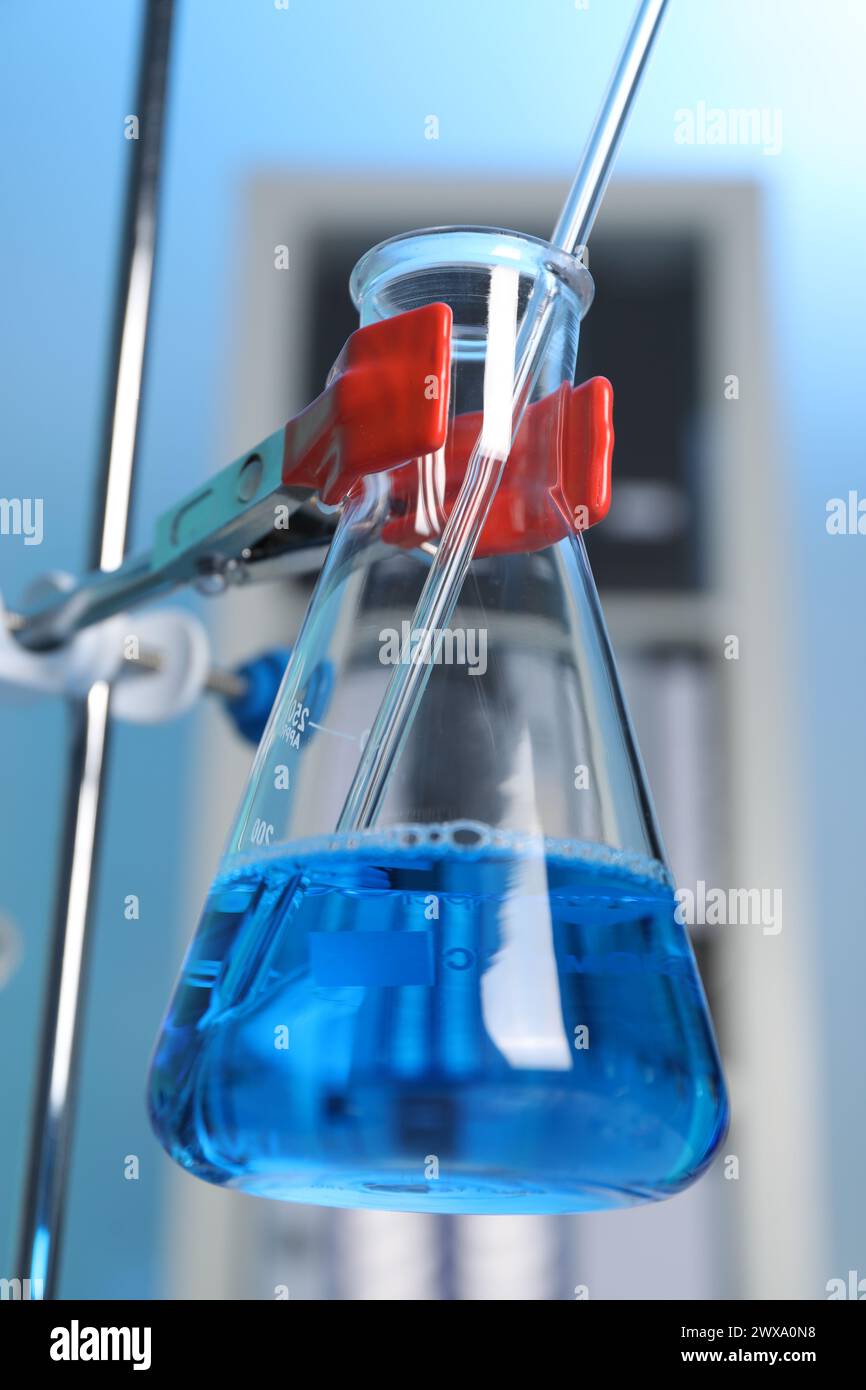 Laboratory analysis. Dripping blue liquid into flask on stand indoors ...
