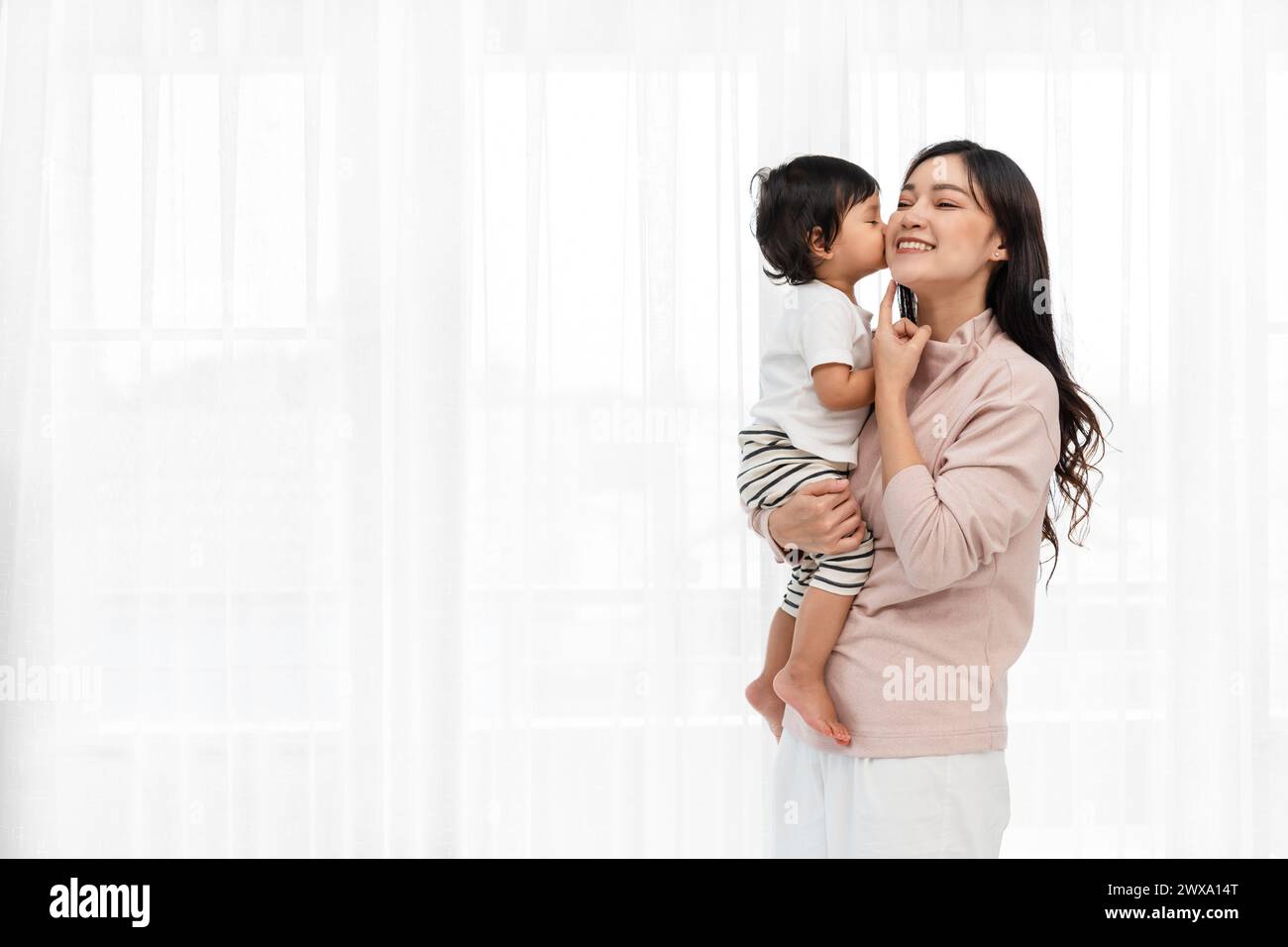 happy mother being kissed by her toddler baby on white window ...