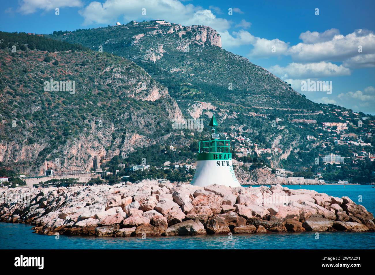 Green and white light house in Beaulieu-sur-Mer, France with mountains ...