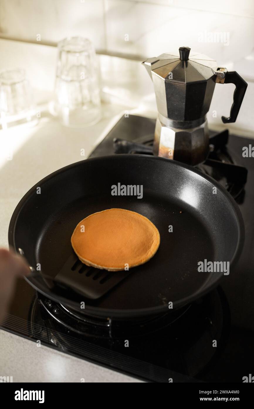 Flipping pancake with spatula, cooking breakfast. Sunlit kitchen Stock ...