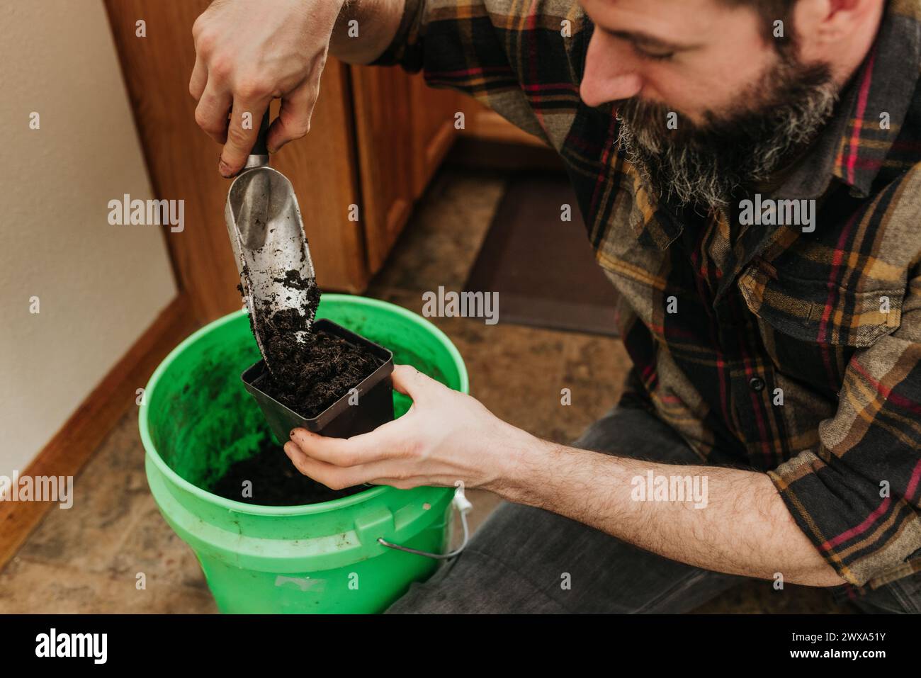 Man scoops fresh dirt from bucket to fill small pot for seedlings Stock ...