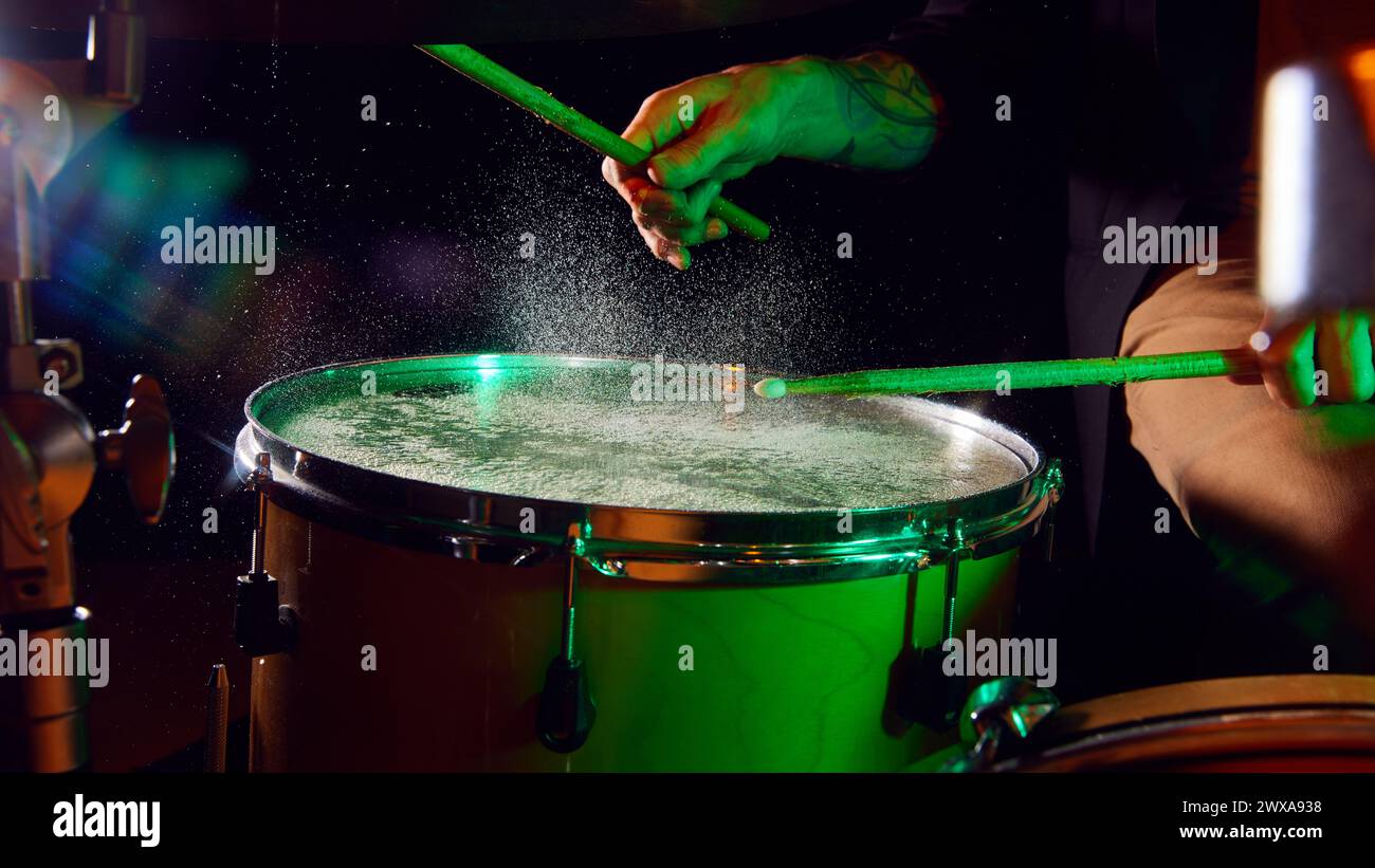 Male hand playing drum with stick on dark background with green hued ...