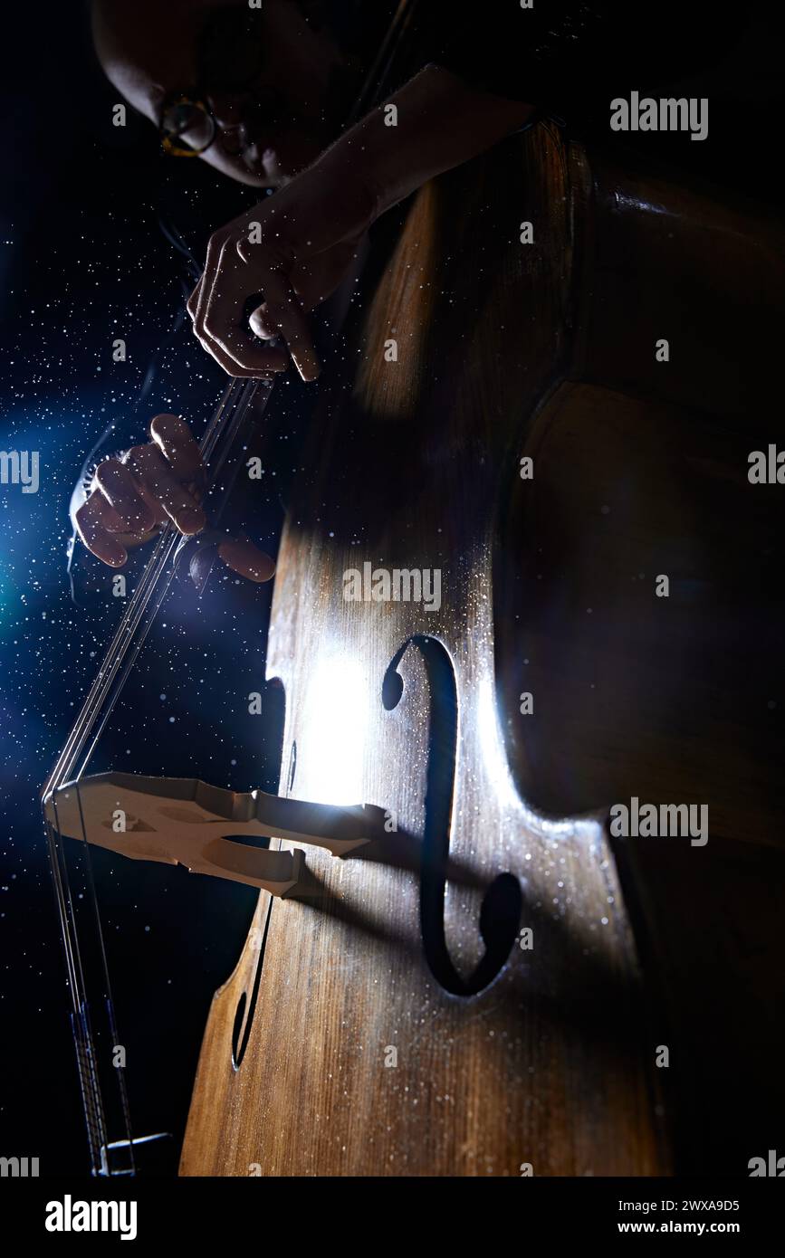 Male musician playing double bass against black background with lights ...