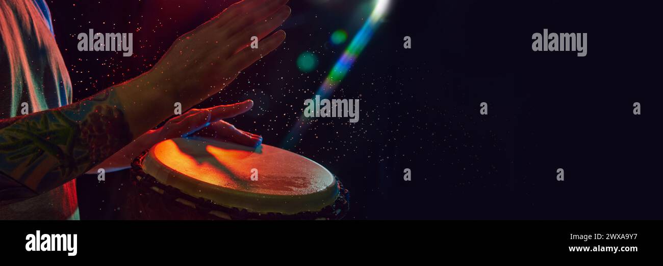 Close-up of male hands, musician playing bongo drums on dark background ...
