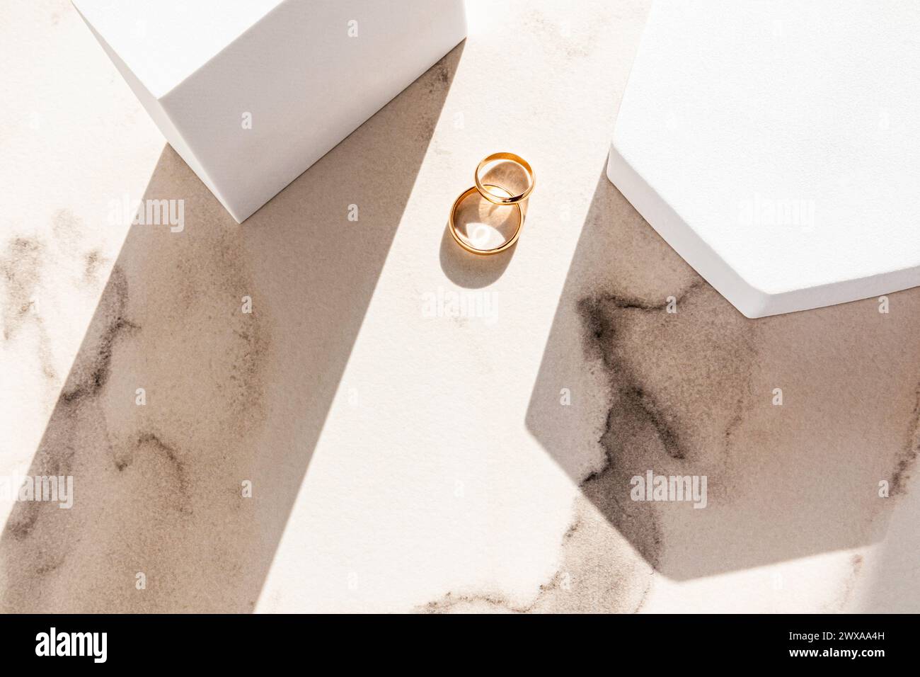 Two classic gold wedding rings lie on a marble beige background between ...