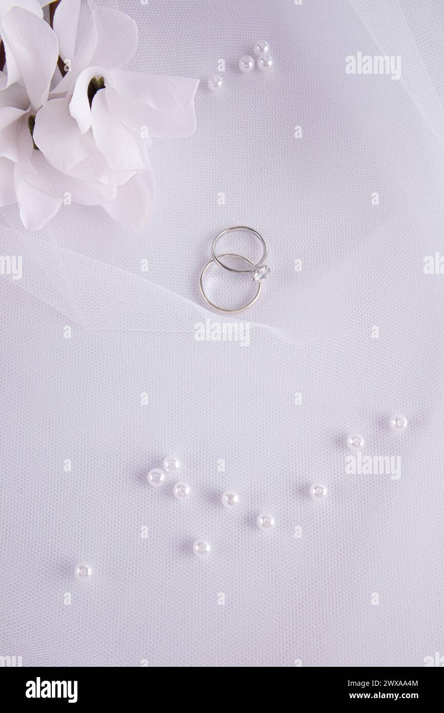 Two white gold and diamond rings lie on a veil with a scattering of ...