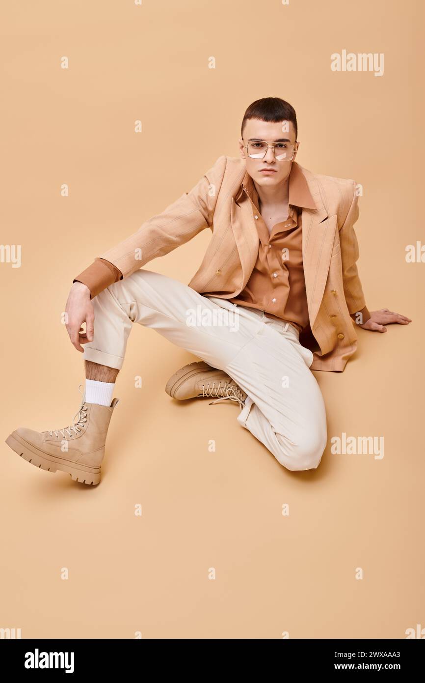 Stylish man in beige jacket and glasses sitting and posing on peachy ...