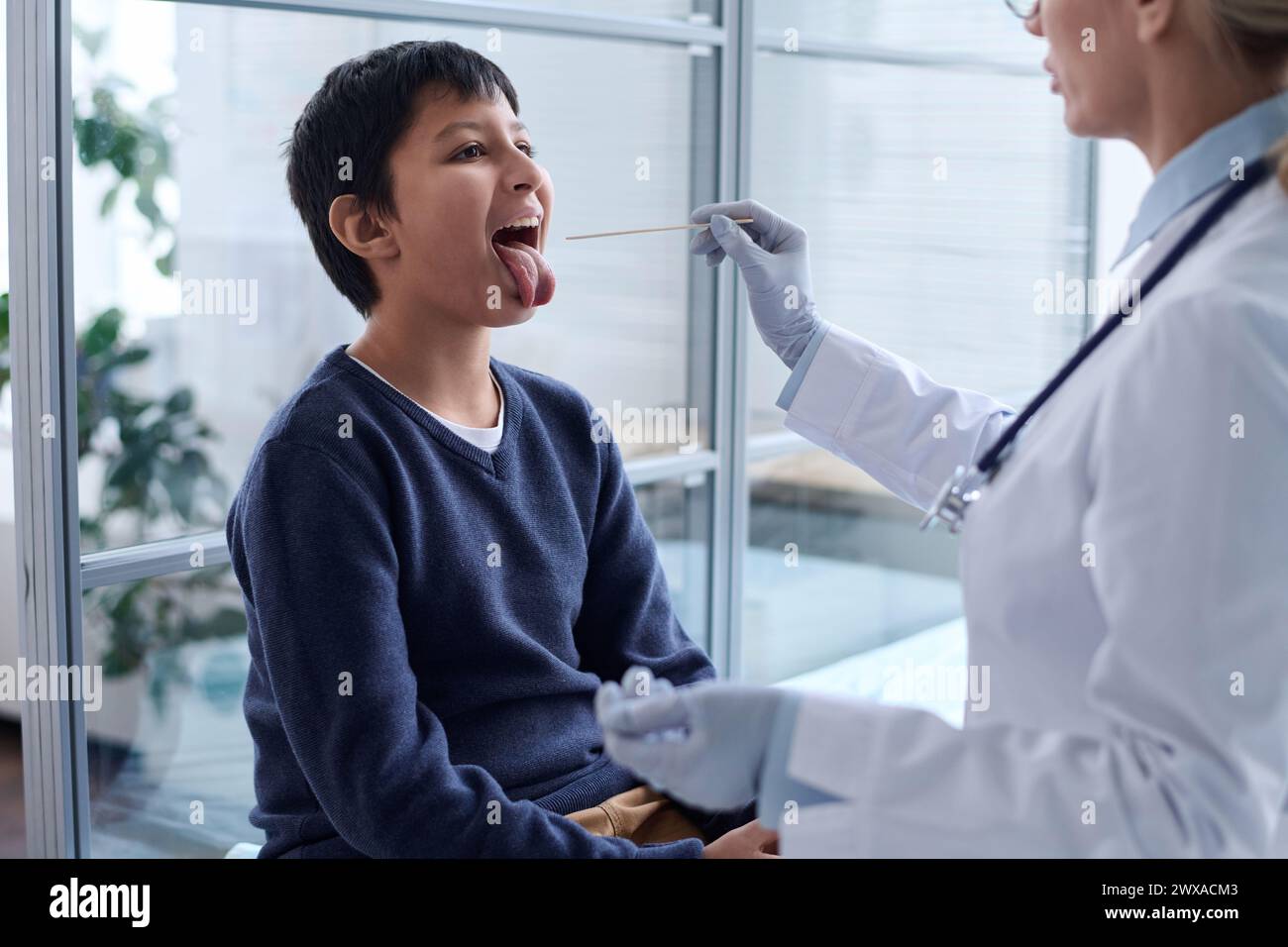 Side view closeup of female doctor doing throat swab of young boy ...