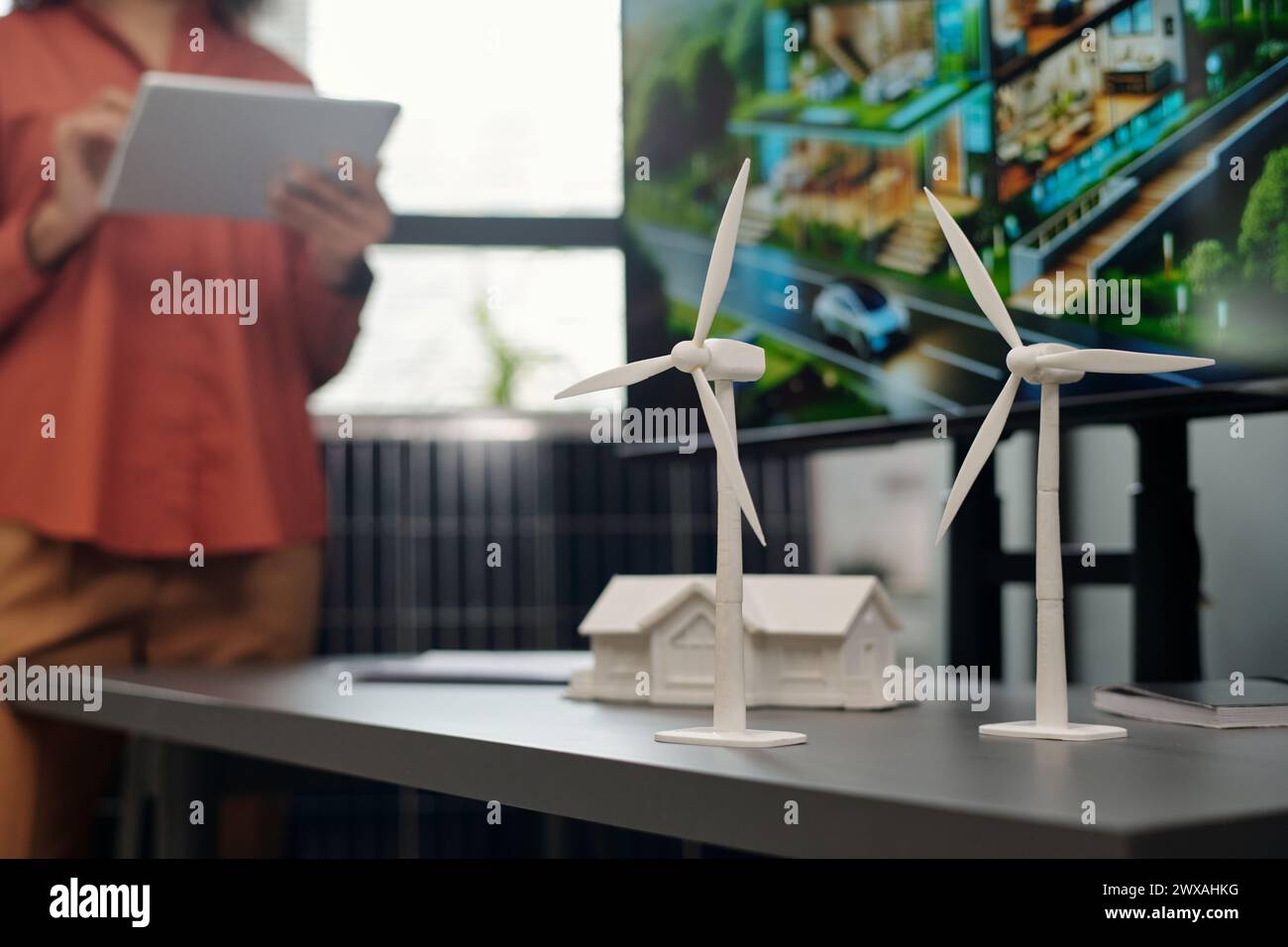 Two windmill models standing on grey desk next to plastic house mockup ...