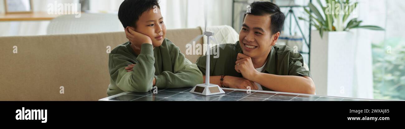 Web banner with father and son looking at small working wind turbine ...
