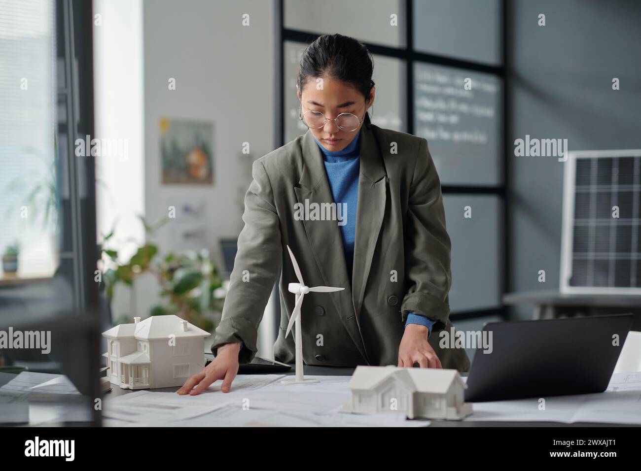Young Asian female architect bending over workplace with blueprint and ...