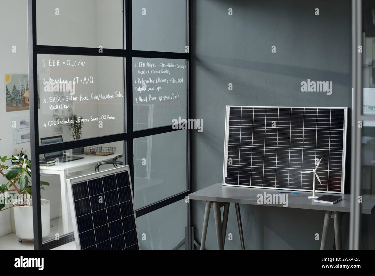 Grey desk with models of solar panel and windmill standing by wall of ...