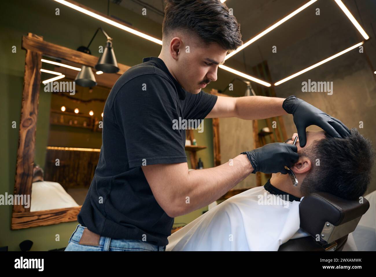 Barber trimming man's beard in barbershop Stock Photo - Alamy