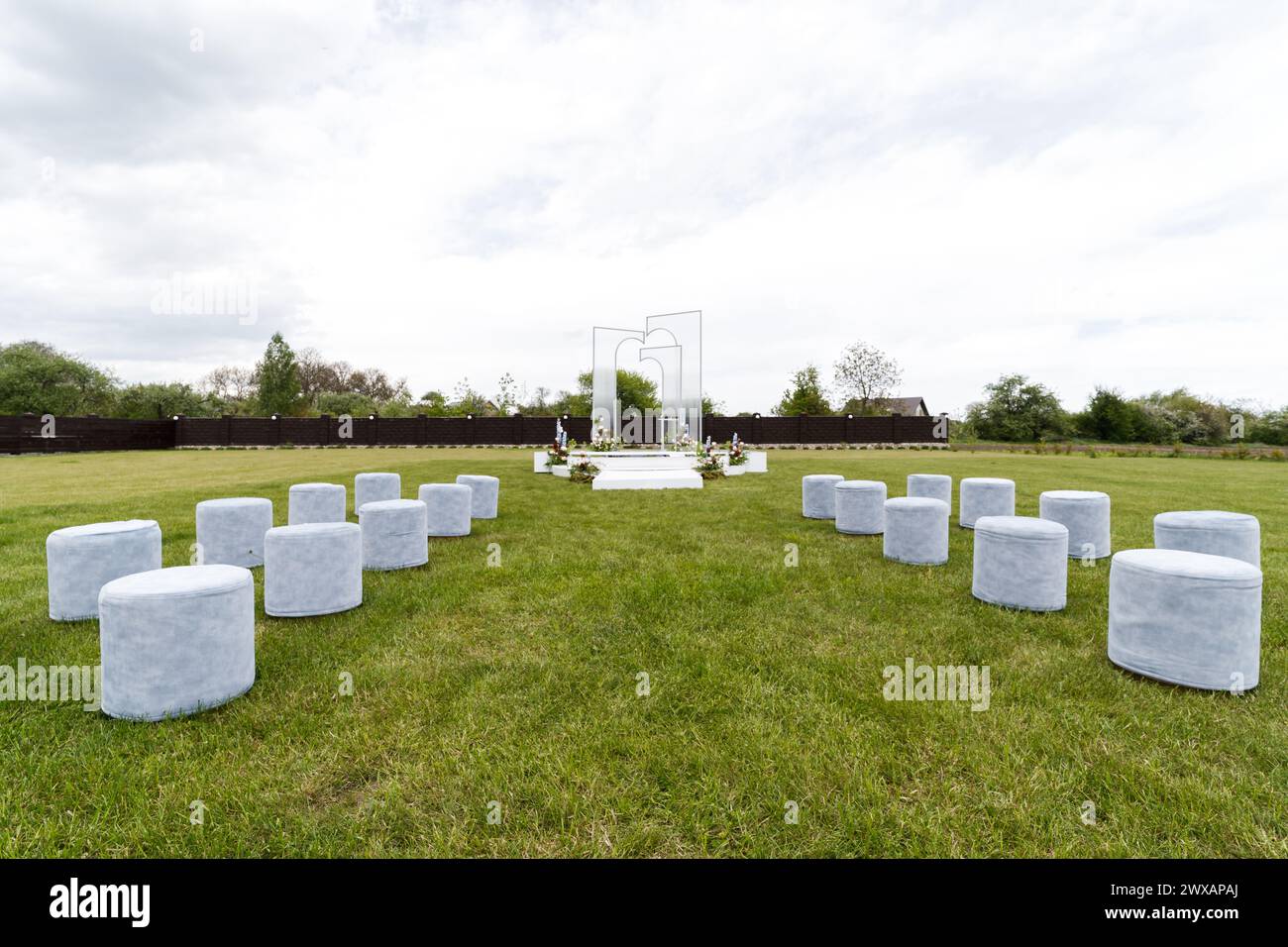 A grassy field featuring a cluster of white stools placed in the center ...