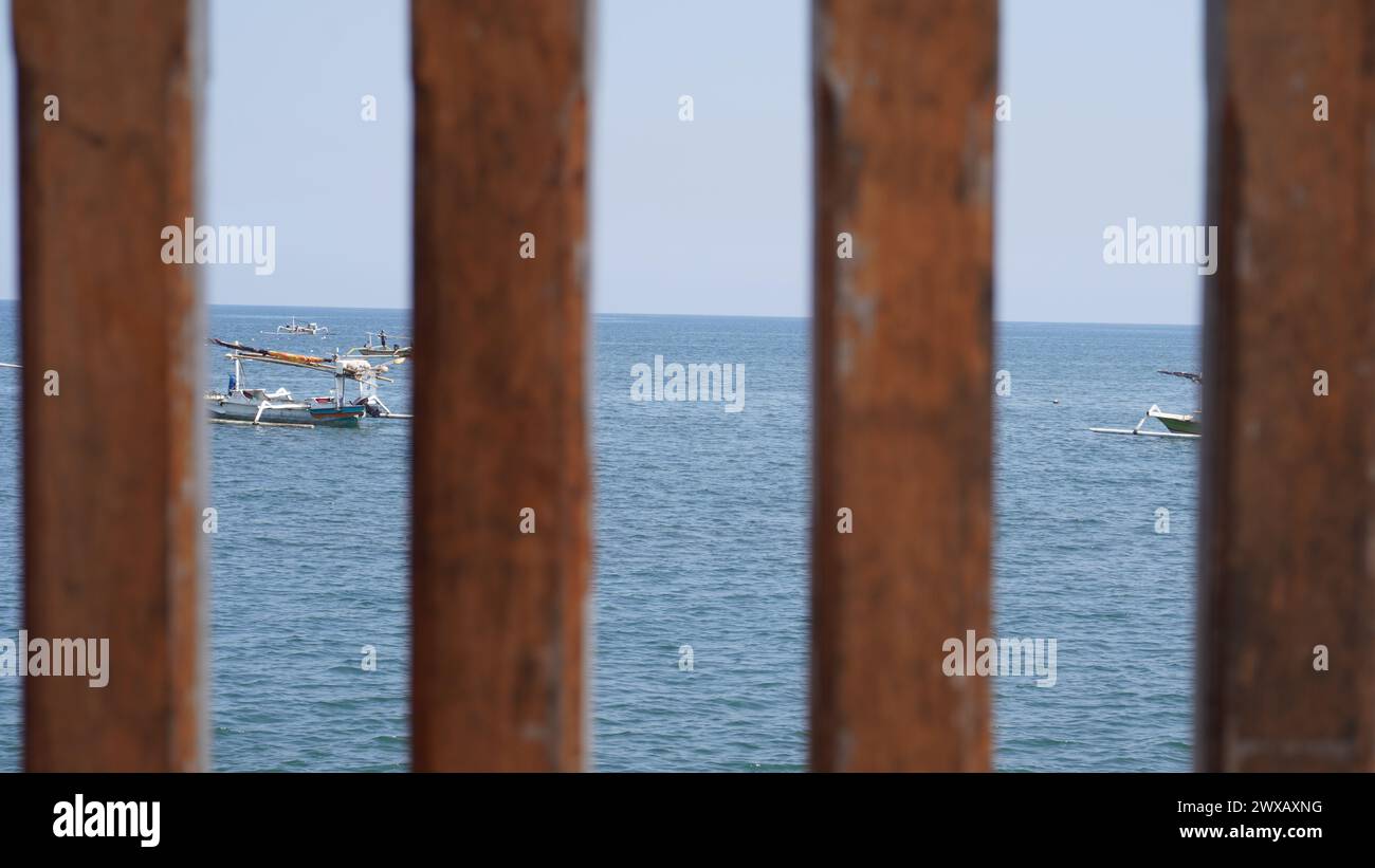 Peeking at the ships sailing on the sea between the wooden frames in Central Lombok, Indonesia ...