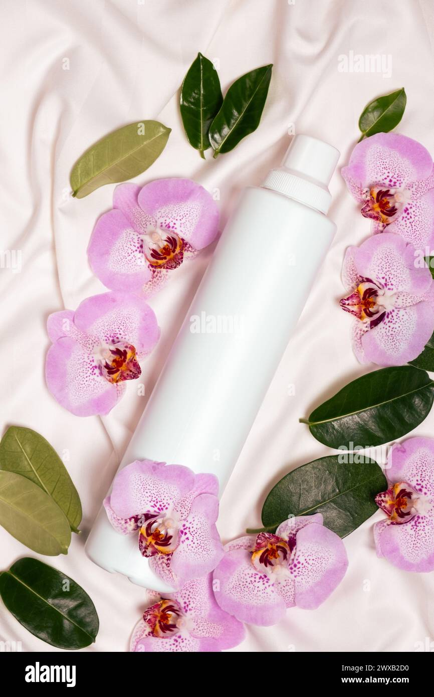 Ecological laundry detergent among orchid flowers on bed linen top view ...