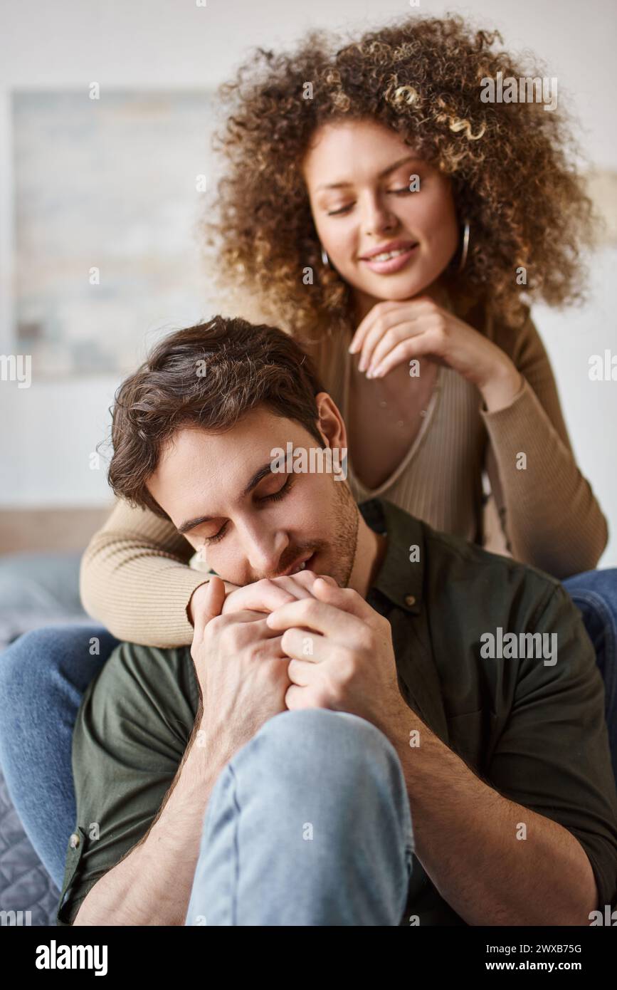 Curly woman hugging her relaxed boyfriend from behind sitting on bed ...