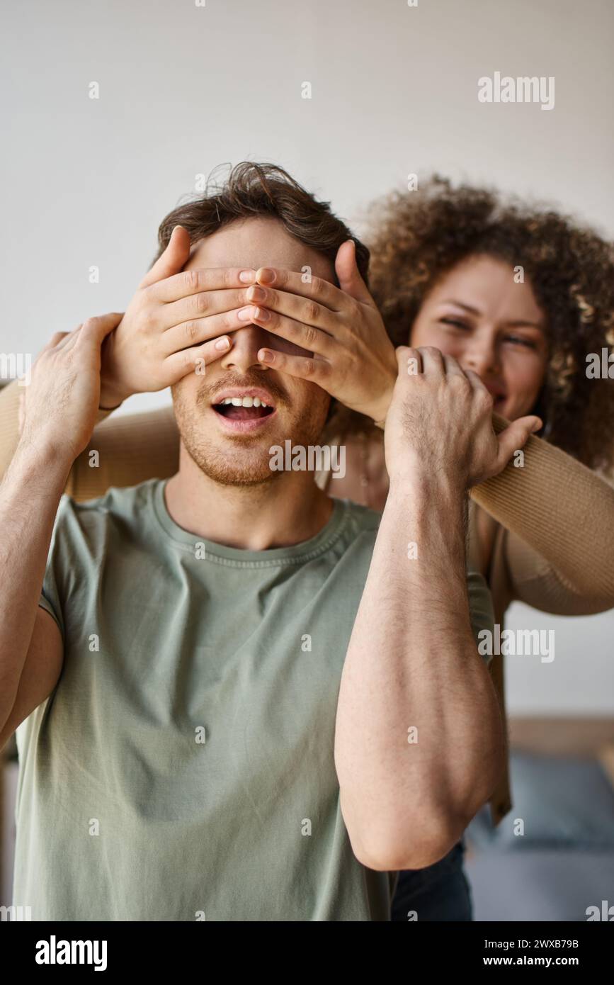 Adoring couple, curly young woman covering eyes of brunette man ...