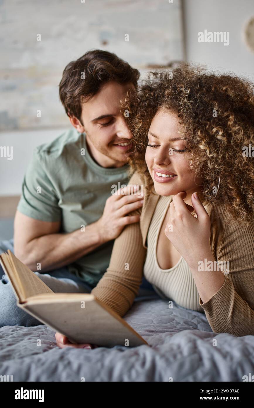 curly young woman finds comfort in her book as brunette man lovingly ...
