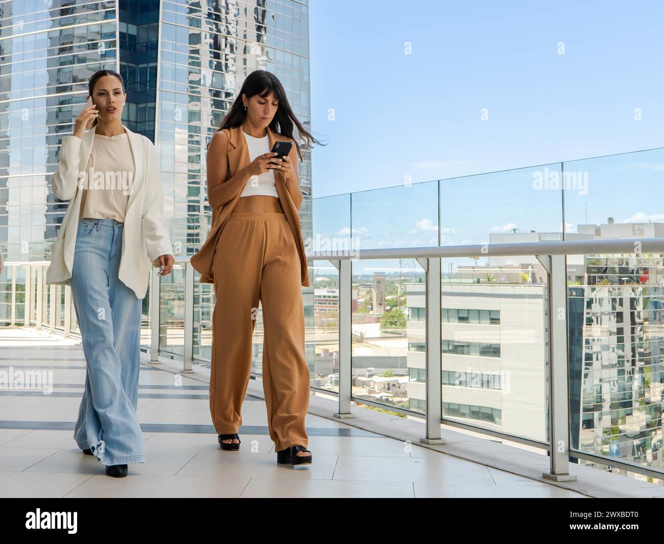 Two women are walking on a glass walkway. One of them is talking on the ...