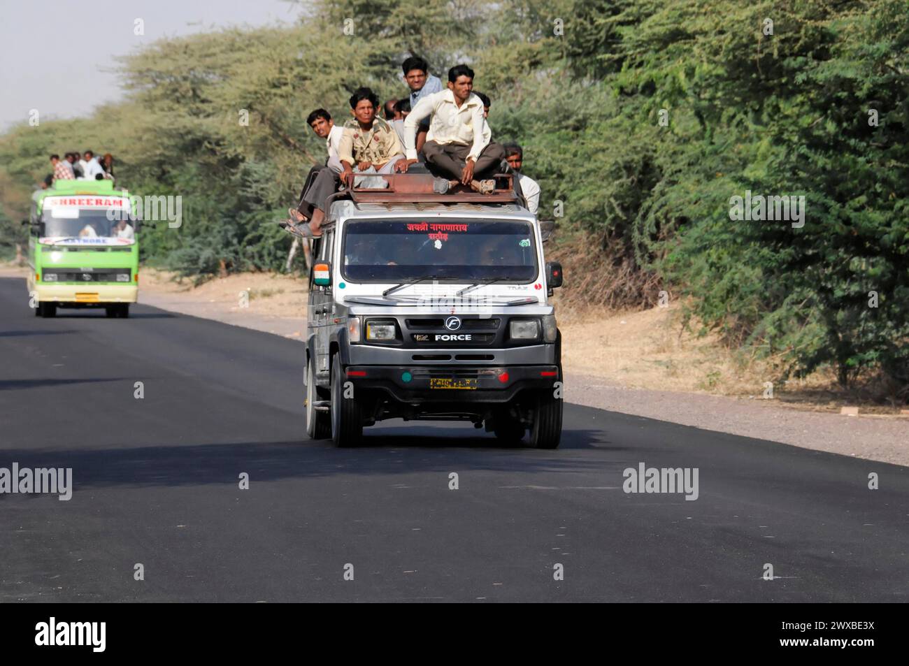 Several people sitting on the roof of an overloaded lorry driving on a ...