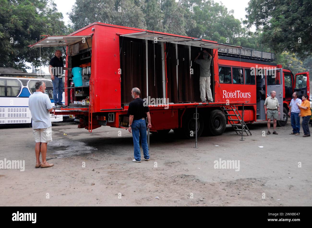 People interacting near a red Rotel Tours bus with open vehicle doors ...