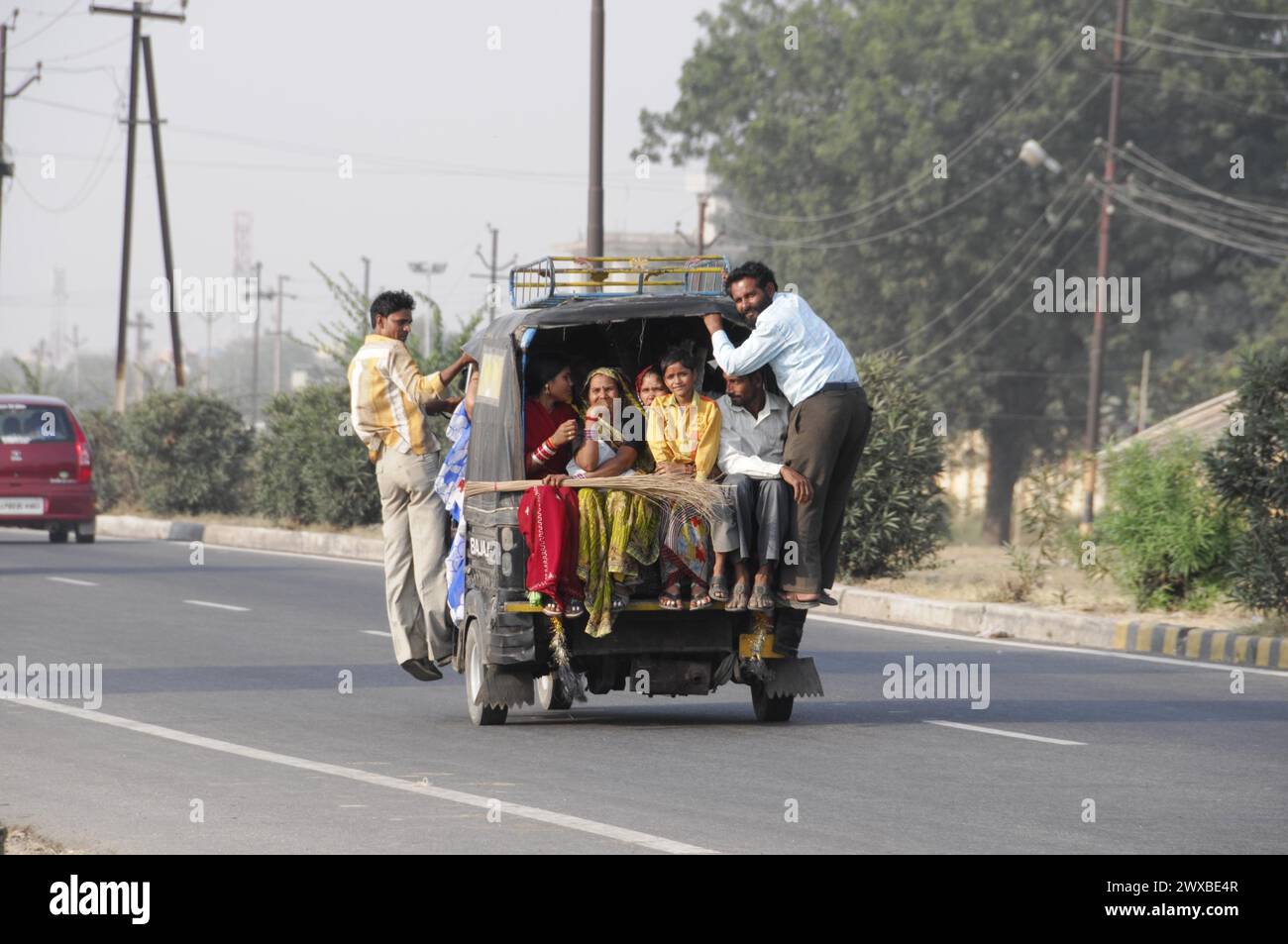 A crowded auto-rickshaw drives on a road in India with passengers ...