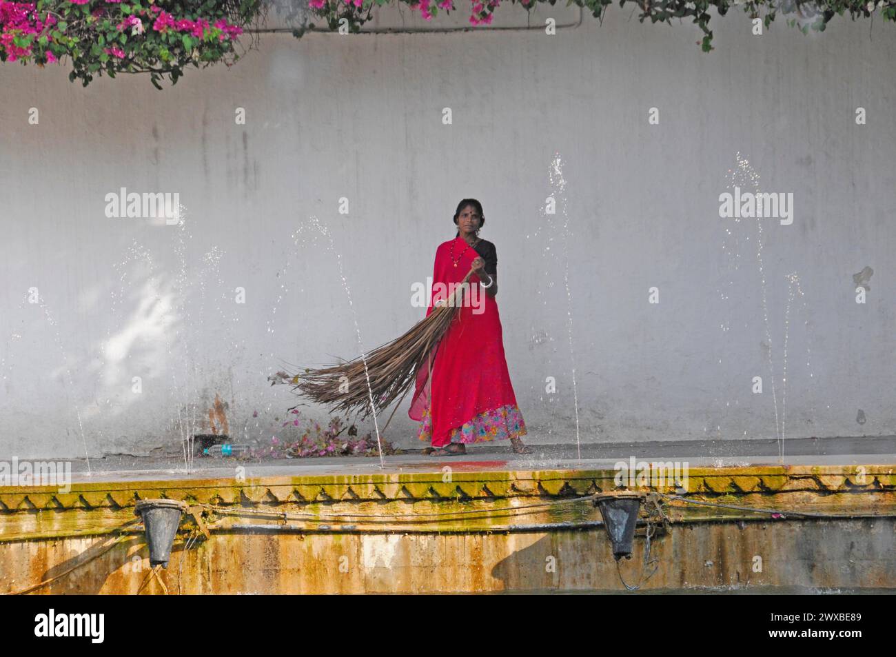 A woman in traditional red dress sweeps the floor next to water ...