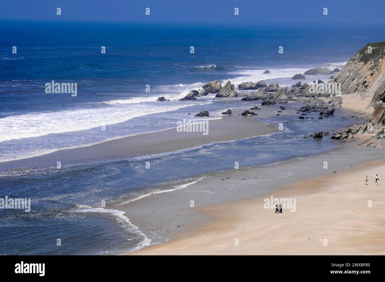 Sandy beach beach with people and wave-like rocks under a cloudless ...